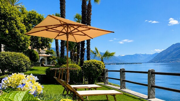 Um jardim à beira do lago com um deque de madeira, uma espreguiçadeira e um guarda-sol.