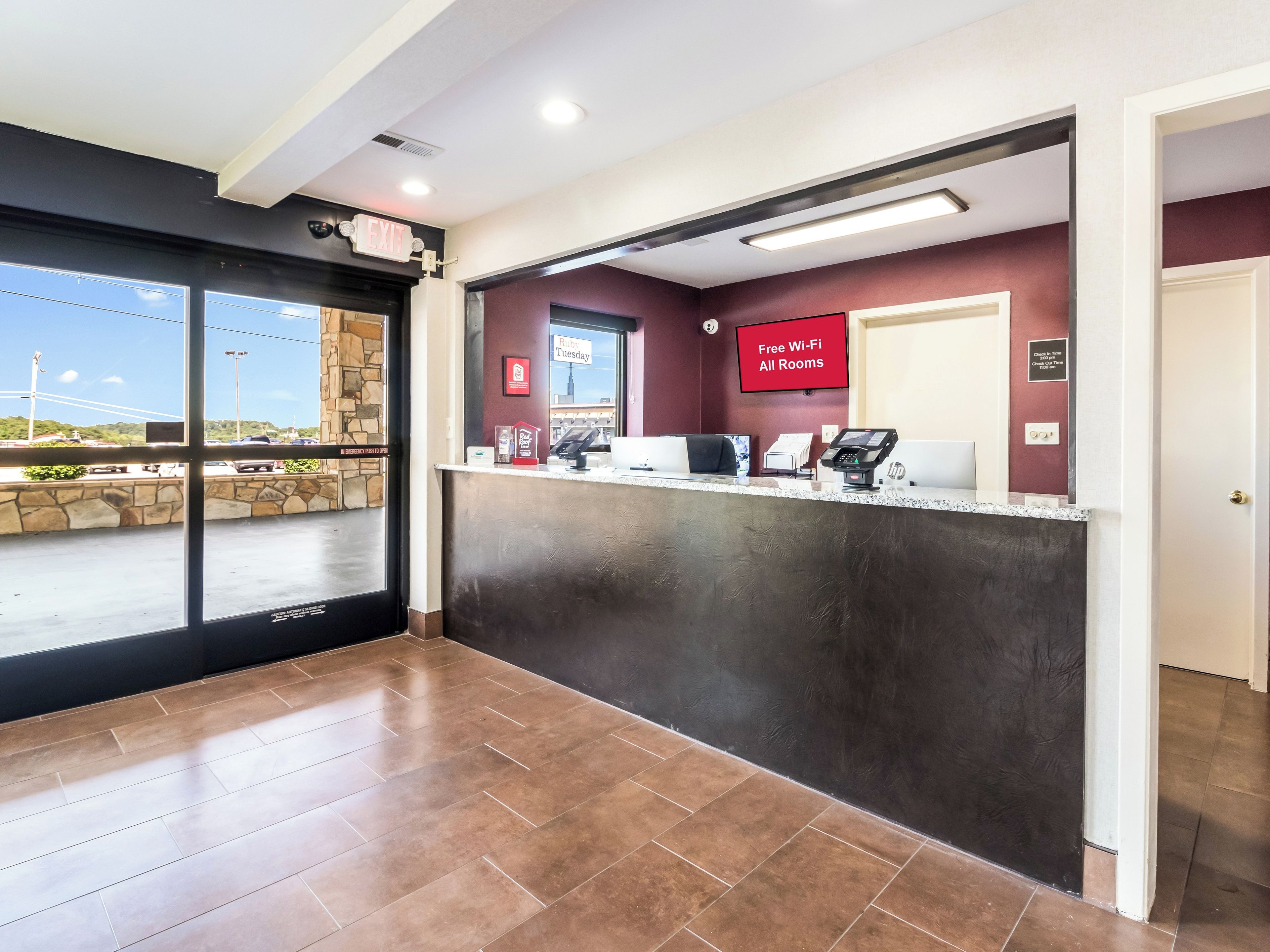 Uma área de recepção de hotel com balcão de check-in, vista para o estacionamento e sinalização indicando Wi-Fi gratuito.