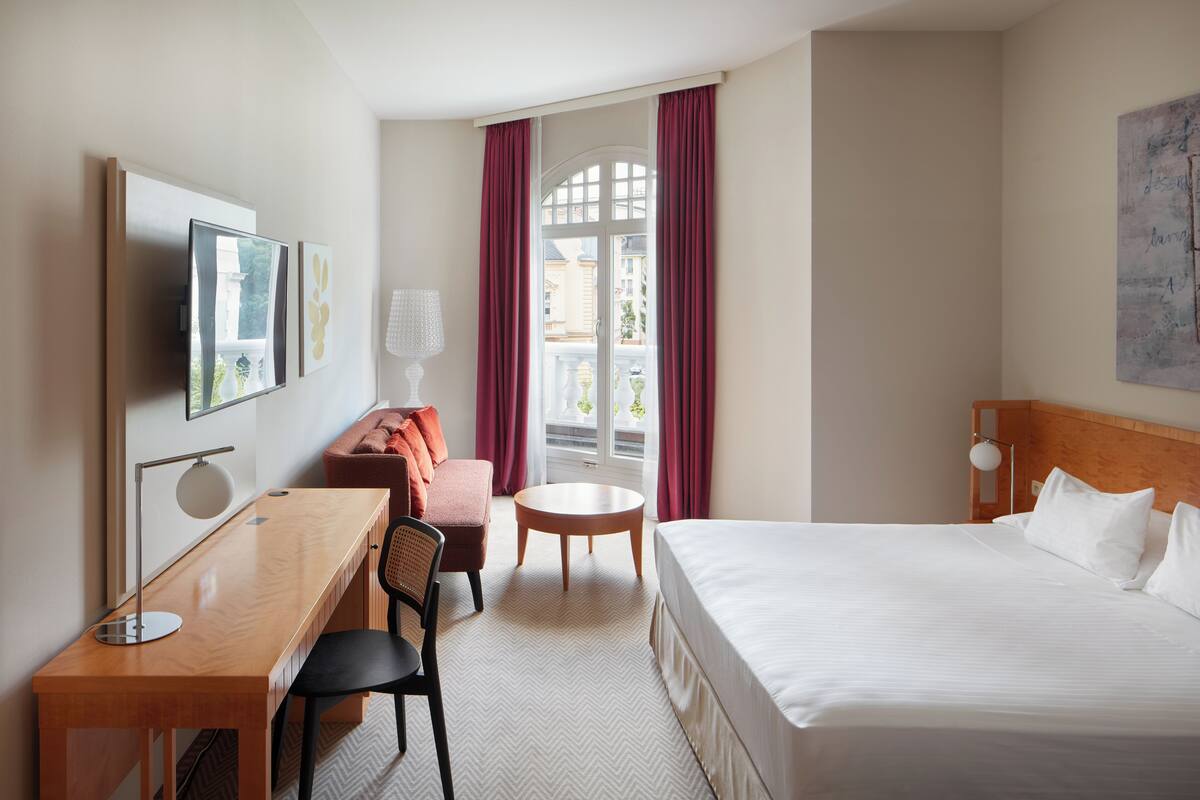 Quarto de hotel com cama, escrivaninha, cadeira e uma pequena mesa.