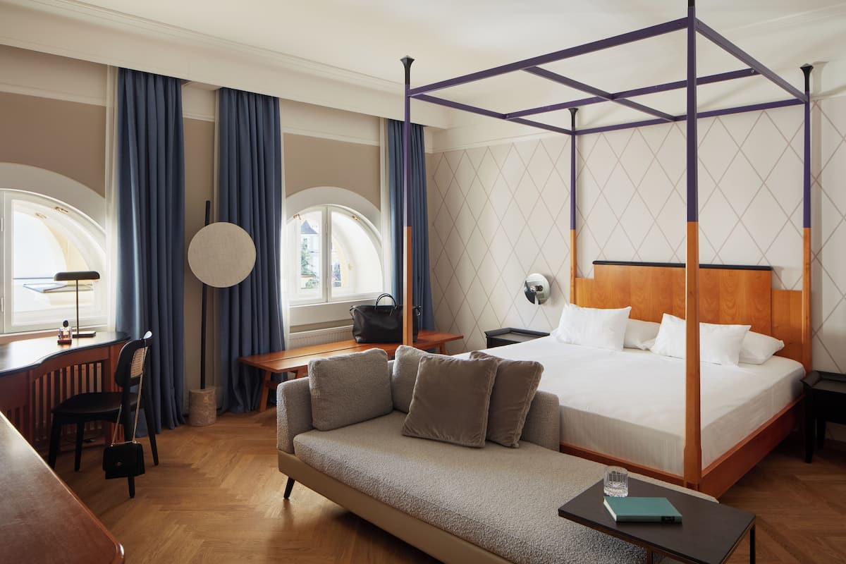 Quarto de hotel com cama de dossel, sofá, escrivaninha com cadeira e uma pequena mesa.