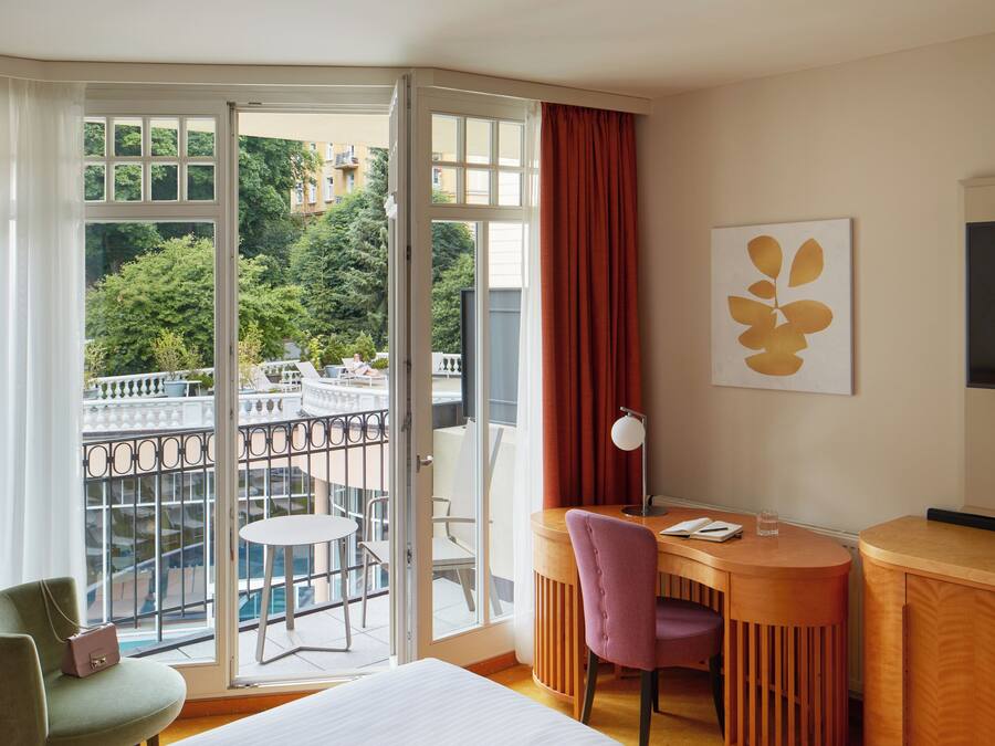 Quarto de hotel com cama, escrivaninha, cadeira, mesa e varanda com vista para a cidade.