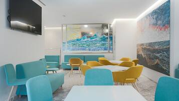 Uma sala de reuniões moderna com mobiliário azul-esverdeado e amarelo, um quadro grande na parede e uma TV de tela plana fixada na parede.