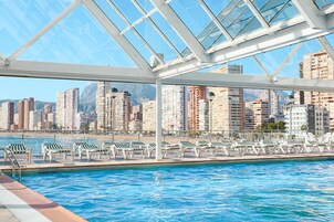 Área de piscina com espreguiçadeiras e vista para a cidade.