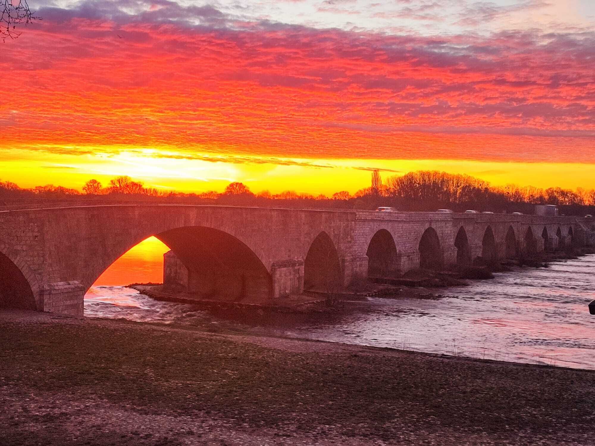 Uma ponte de pedra com várias arcos sobre um rio ao pôr do sol.
