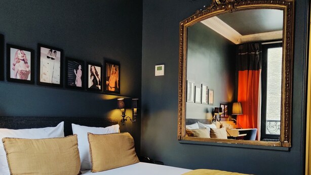 Quarto de hotel com uma cama grande, um espelho amplo e quadros nas paredes.