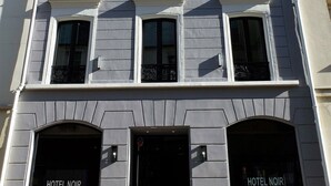 Fachada de edifício com três grandes janelas e duas portas em arco, cada uma com a inscrição 