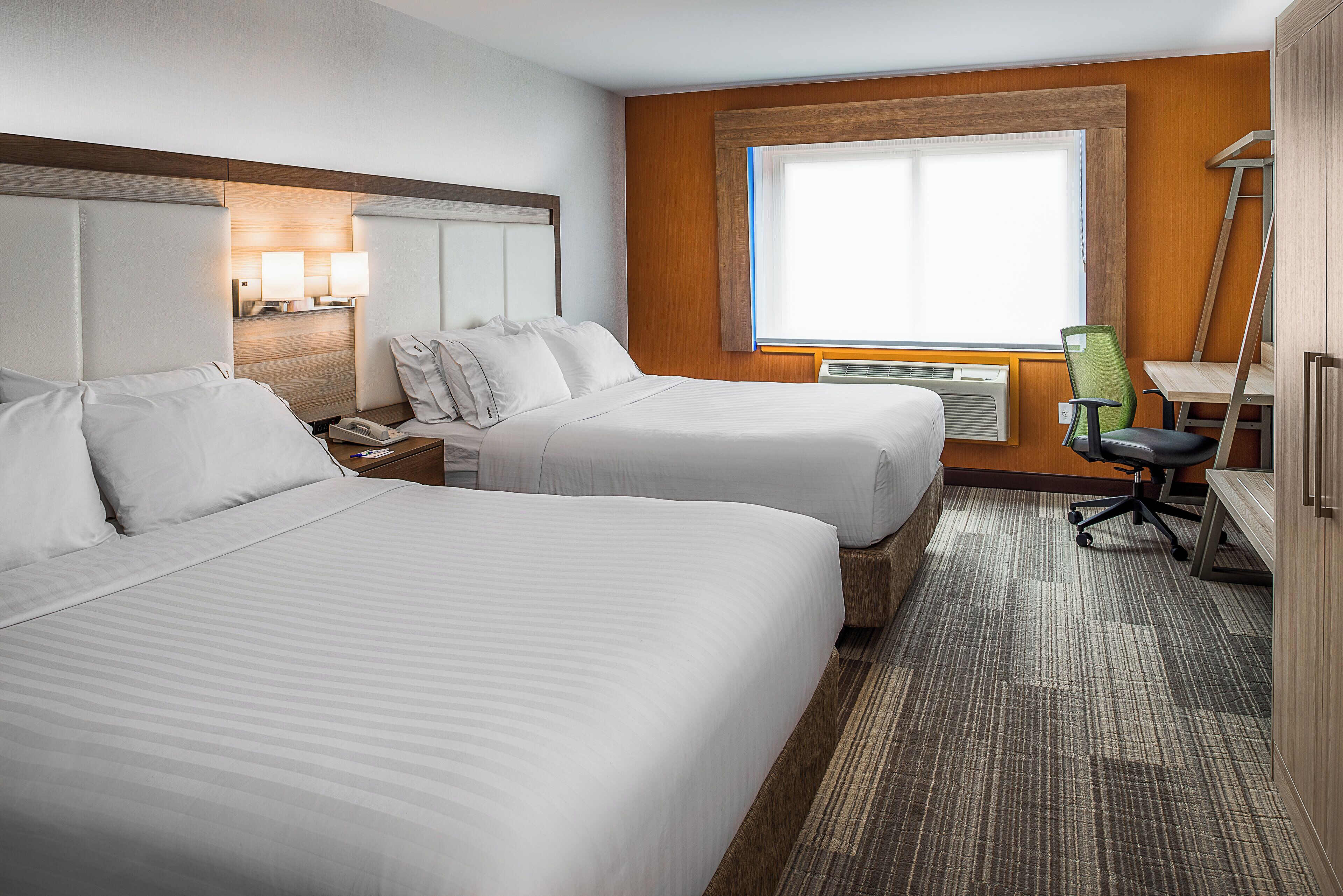 Quarto de hotel com duas camas, uma escrivaninha, uma cadeira, um abajur e uma janela.