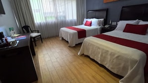 Quarto de hotel com duas camas, uma escrivaninha, uma cadeira e uma janela com cortinas.