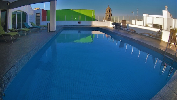 Piscina com espreguiçadeiras e vista para o campanário de uma igreja.