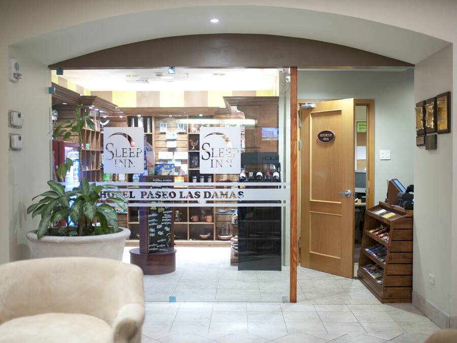 Entrada de hotel com placa da Sleep Inn, um vaso de planta, uma estante de madeira e piso de azulejos.