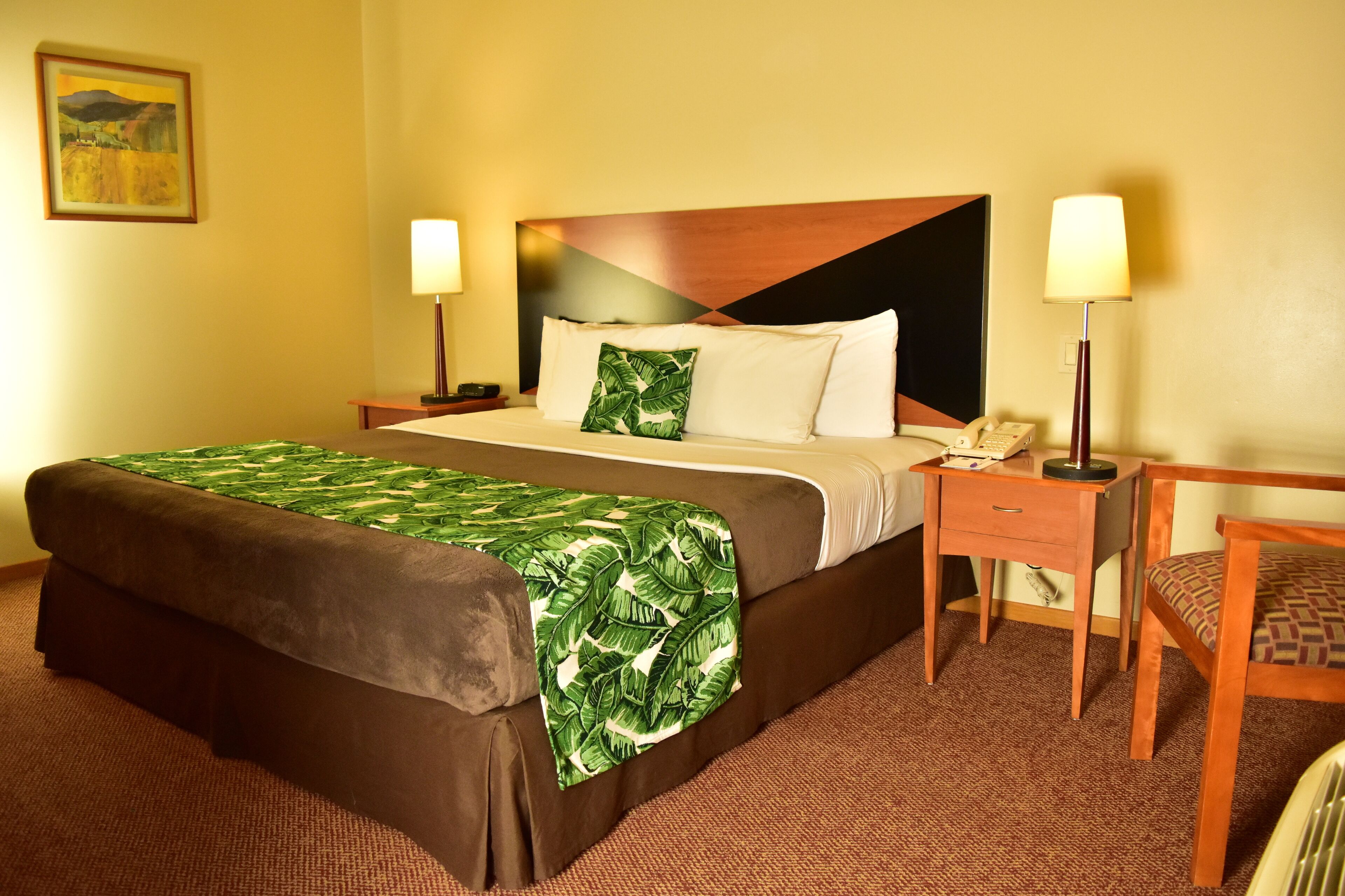 Quarto de hotel com cama, mesas de cabeceira, escrivaninha e uma cadeira.