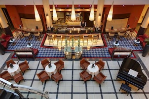 Um hall de hotel com área de bar, diversos arranjos de assentos e um piano de cauda.