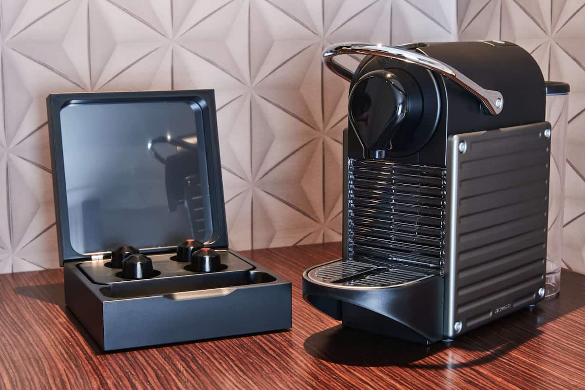 Máquina de café e chaleira sobre uma superfície de madeira, com parede ao fundo em padrão geométrico.