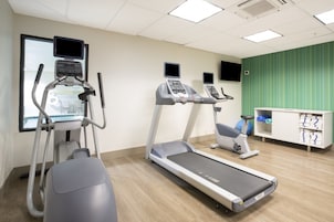 Uma sala de ginástica com esteiras, elípticos e um armário de armazenamento.
