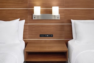 Quarto de hotel com duas camas, uma mesa de cabeceira, luminária fixada na parede e painel de controle.