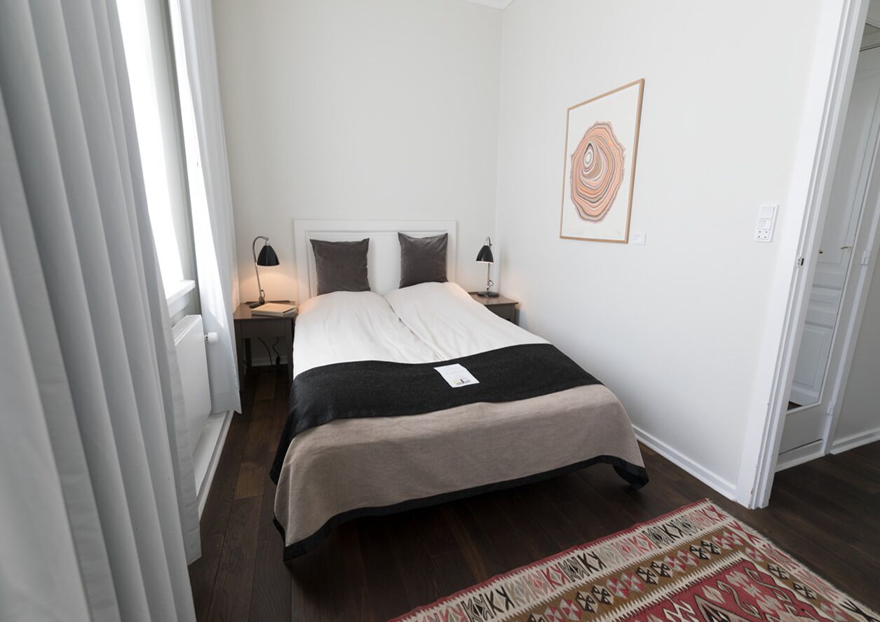 Quarto arrumado com cama, abajures, tapete e uma obra de arte na parede.