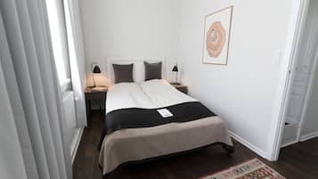 Quarto arrumado com cama, abajures, tapete e uma obra de arte na parede.