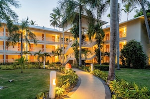 Hotel de vários andares com pátio central, palmeiras e um caminho que leva à entrada.