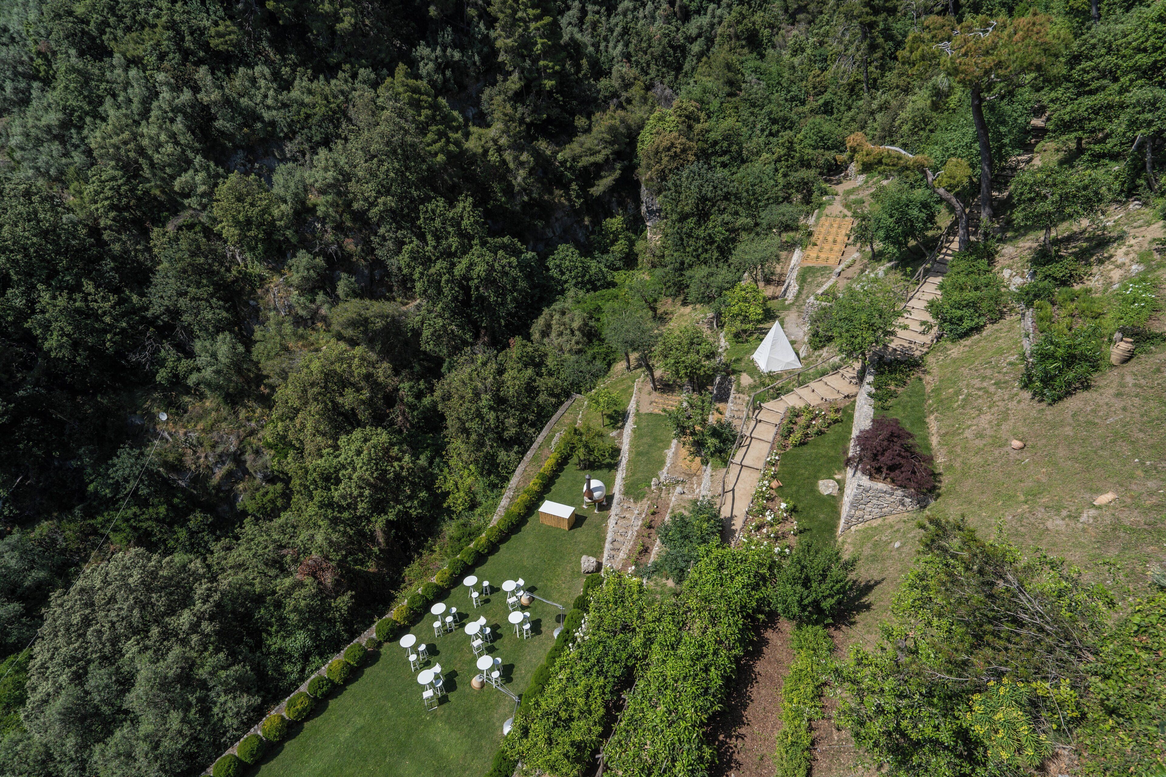Vista aérea de um terreno com área gramada, algumas estruturas brancas e um muro de pedra.