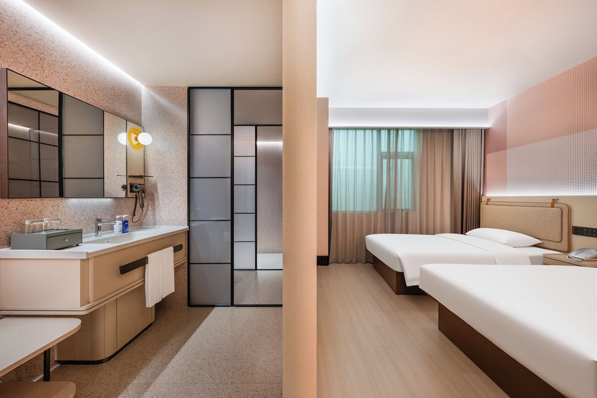 Quarto de hotel com banheiro, uma cama, mesa de cabeceira e criado-mudo.