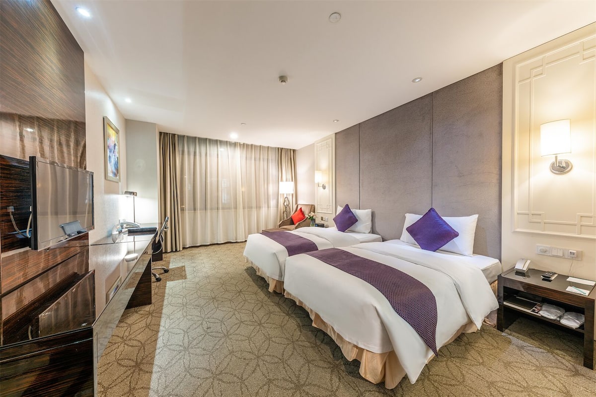 Quarto de hotel com duas camas, televisão, escrivaninha e abajur.