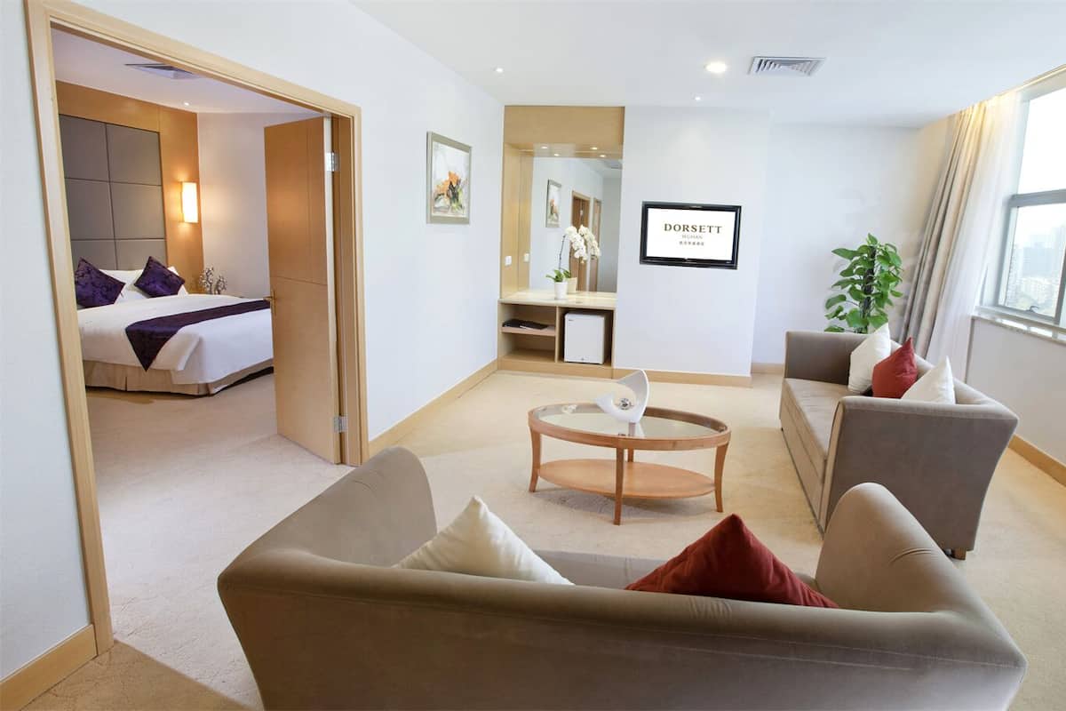 Quarto de hotel moderno com cama, sofá, mesa de centro, espelho e vista para a cidade.