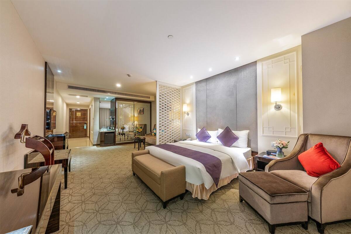Quarto de hotel com uma cama, escrivaninha, cadeira e uma mesinha.