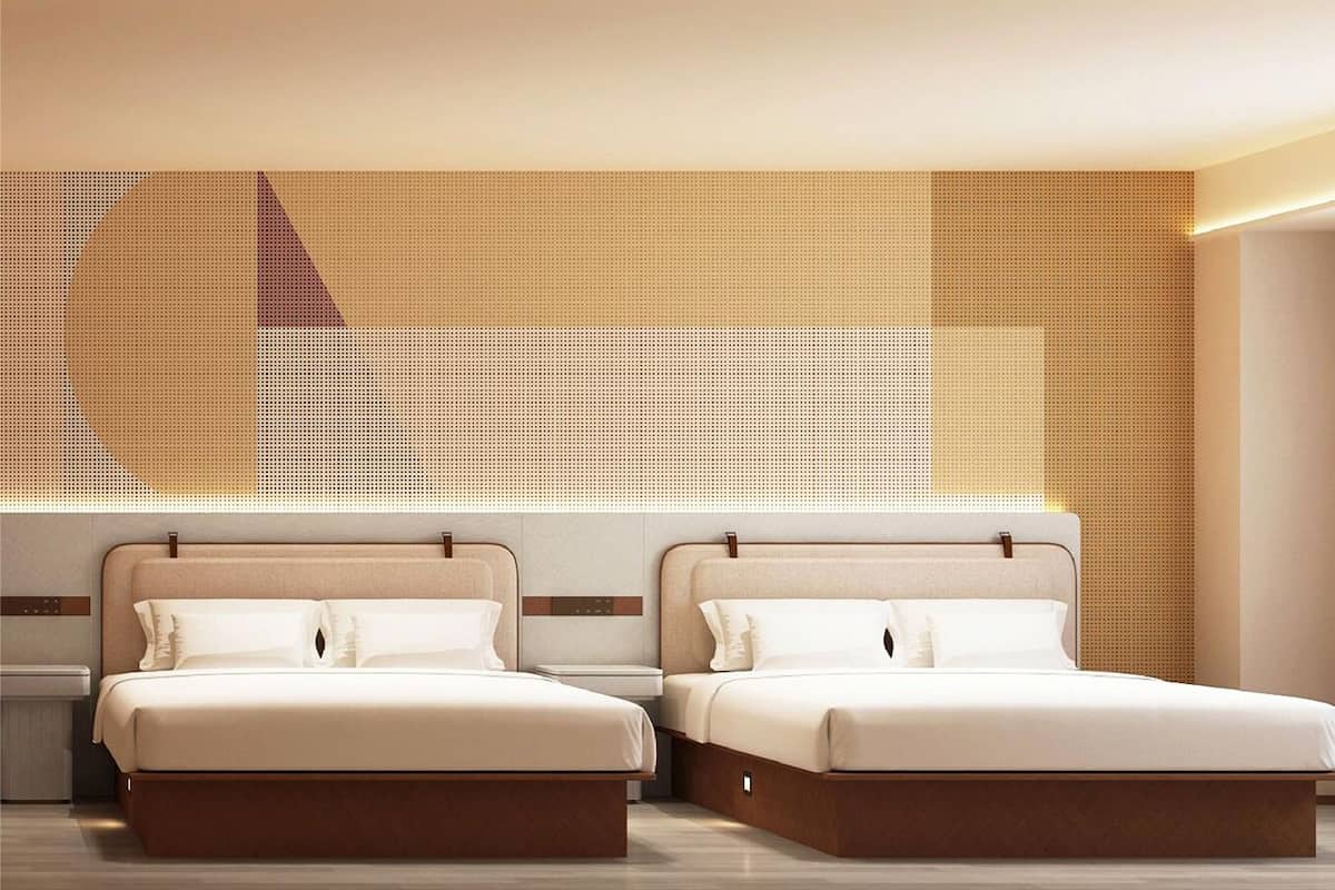 Quarto de hotel com duas camas, uma janela grande com cortinas e uma parede com padrão geométrico.