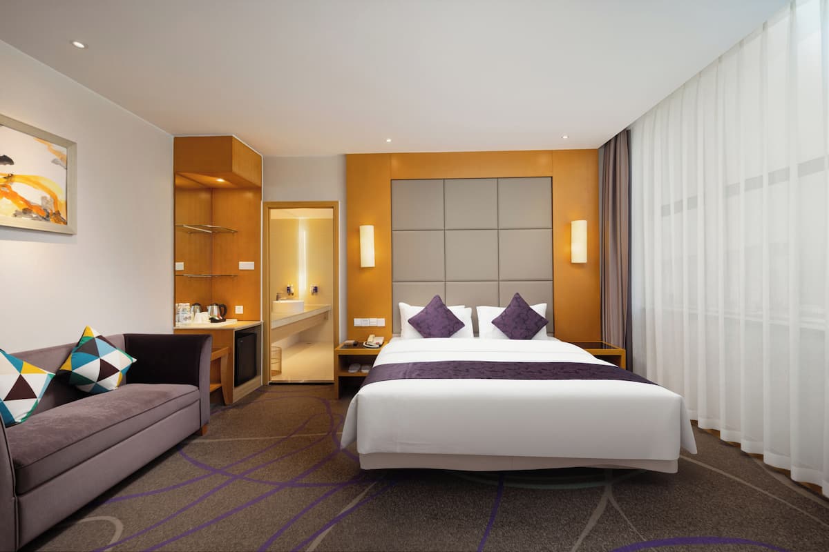 Quarto de hotel com cama, sofá, escrivaninha, espelho e banheiro.