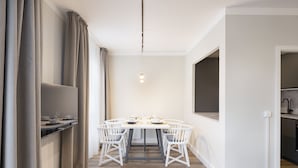 Uma cozinha moderna com armários brancos, uma mesa de jantar com cadeiras e uma janela que oferece luz natural.