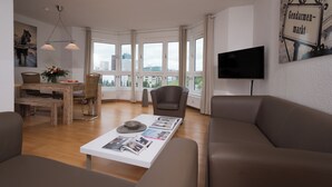 Uma sala de estar moderna com área de jantar, janelas amplas, televisão de tela plana e vista para a cidade.