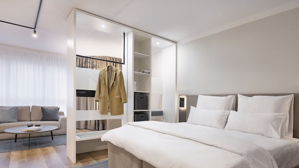 Quarto de hotel moderno com cama, sofá, mesa de centro e closet espaçoso.