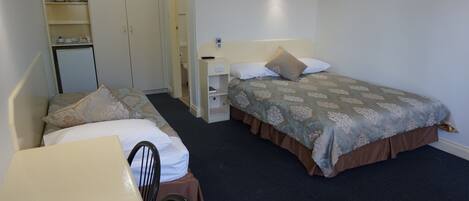 Quarto de hotel com duas camas, uma escrivaninha, uma cadeira, um guarda-roupa e uma pequena cozinha equipada.