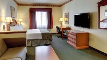Quarto de hotel com cama, escrivaninha, televisão, cômoda e sofá.