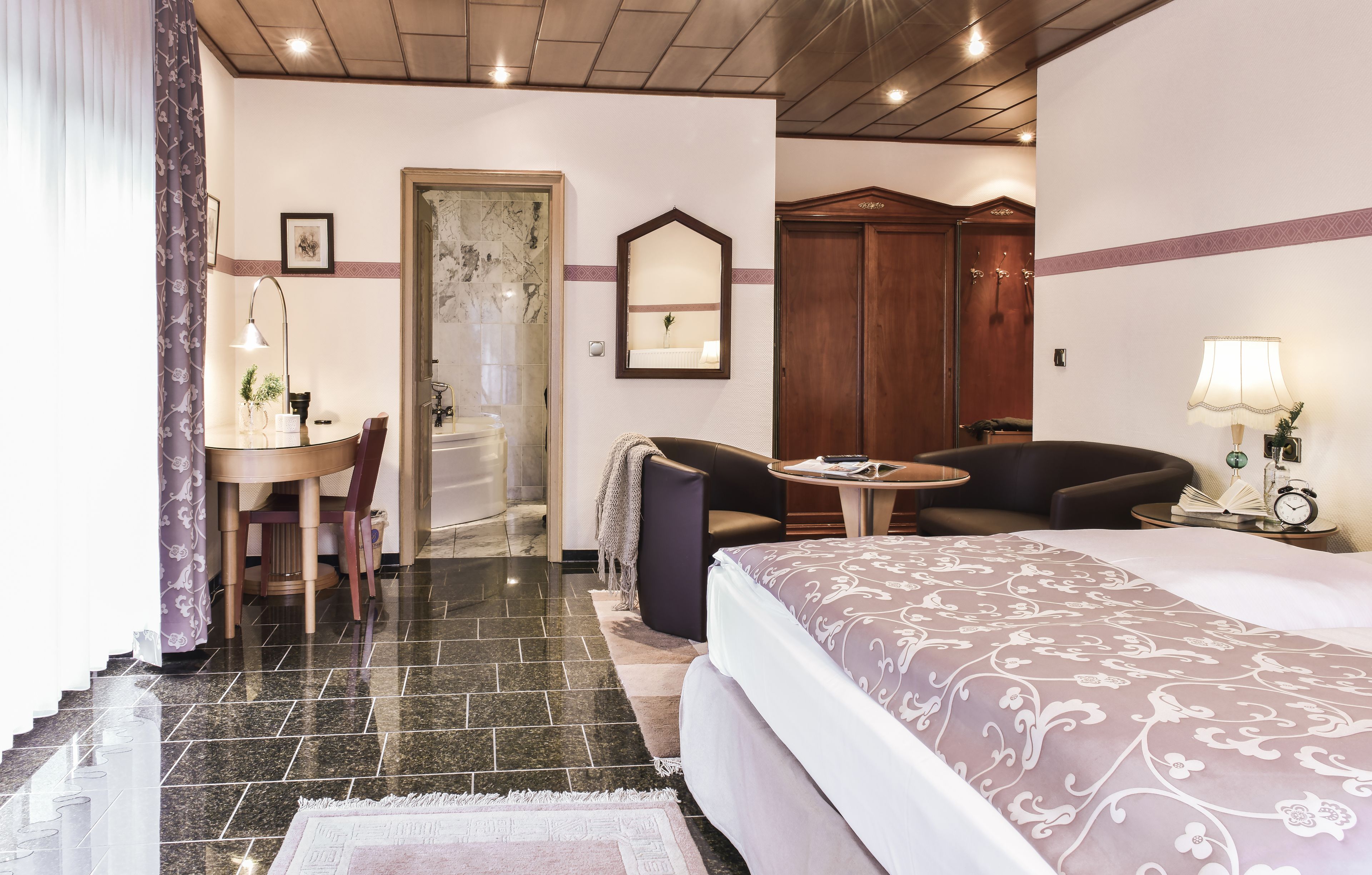 Quarto de hotel com uma cama, uma mesa com cadeira, uma mesinha, um armário e um espelho na parede.