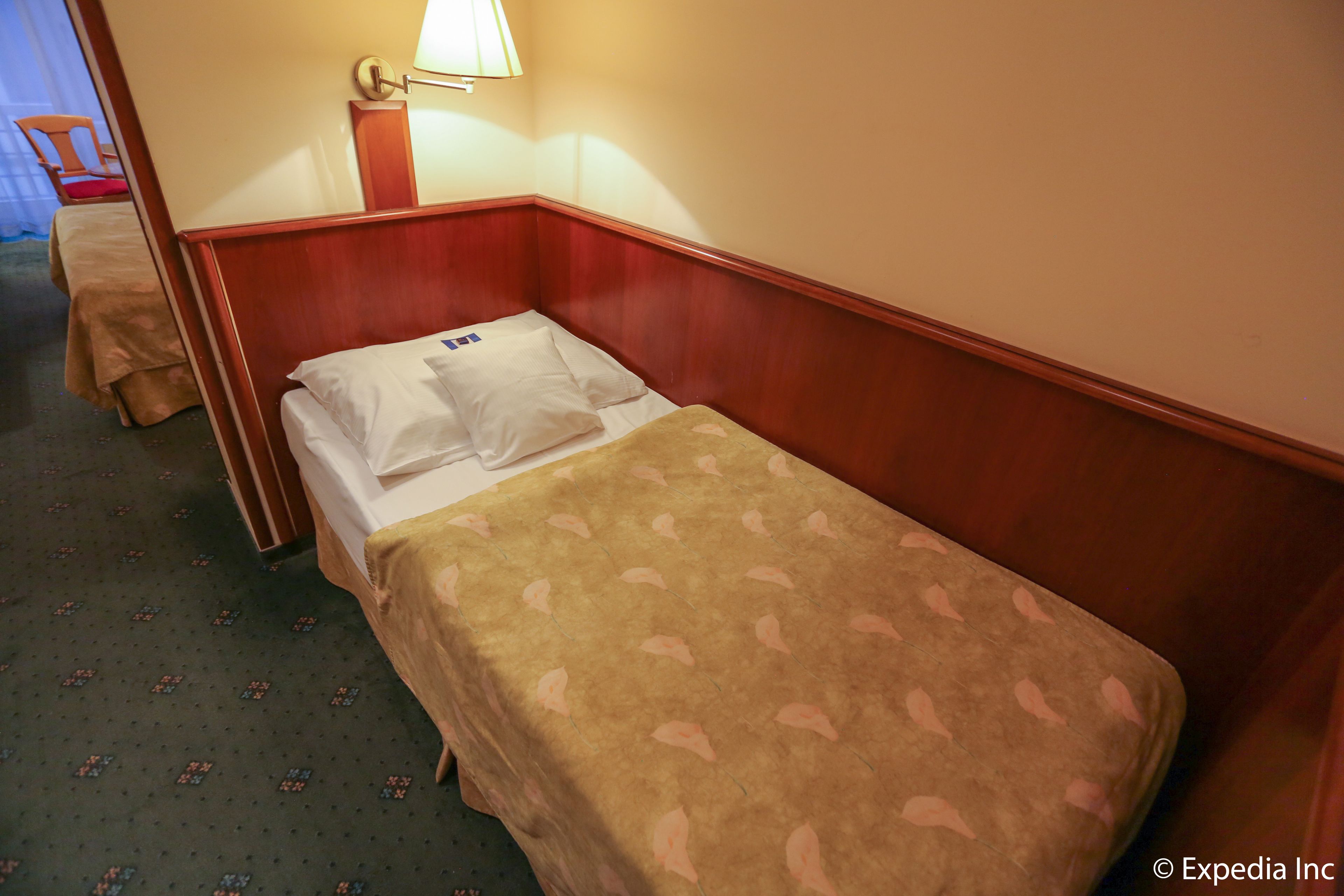 Uma cama de solteiro com colcha estampada, cabeceira de madeira e mesa de cabeceira com abajur.