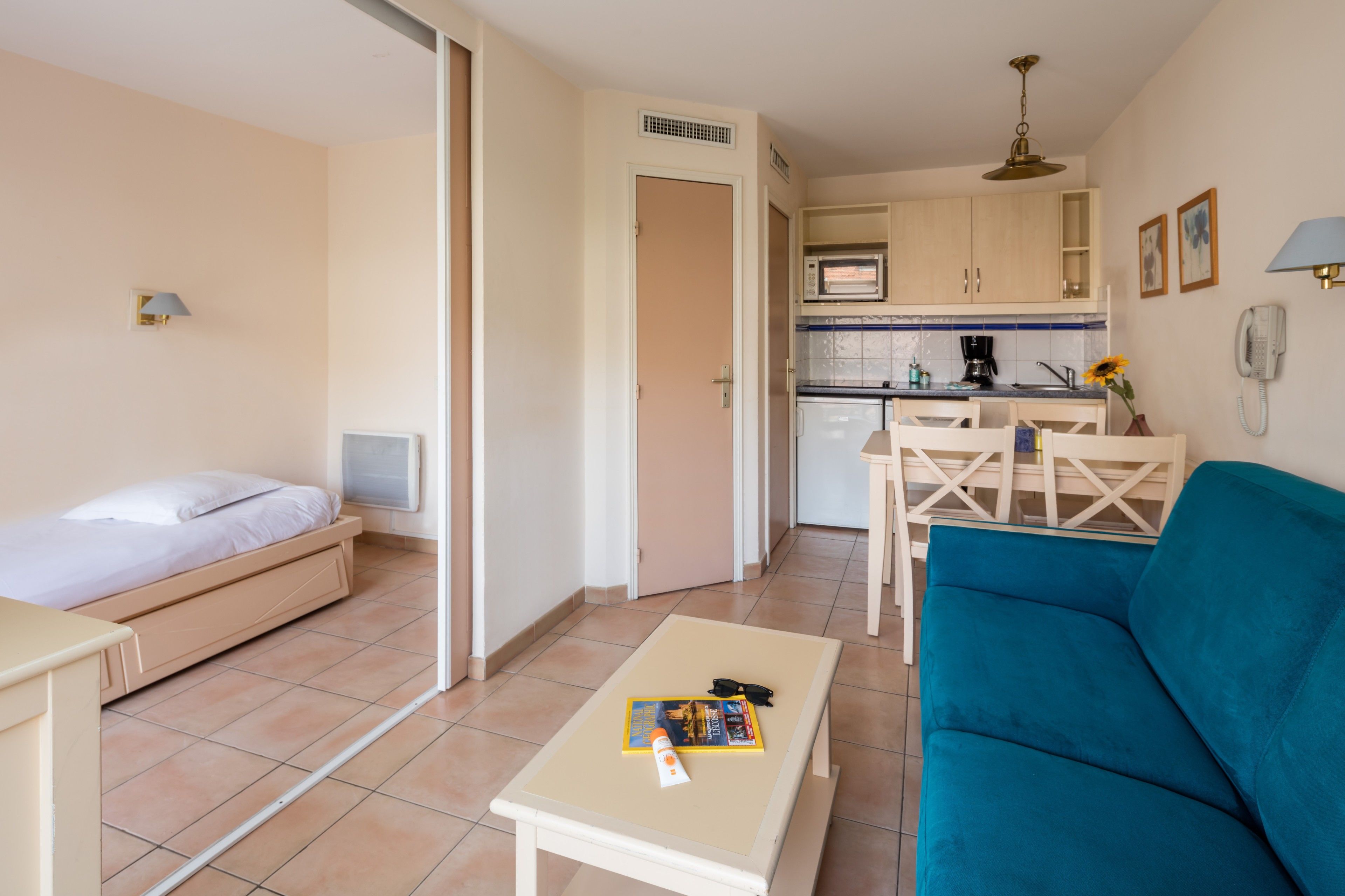 Quarto de hotel compacto com cama, uma mesa pequena, sofá, cozinha compacta e banheiro.
