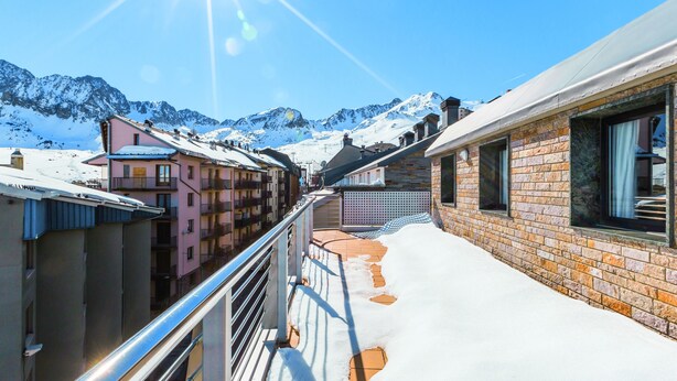 Varanda coberta de neve com vista para a montanha, um edifício de tijolo e um edifício rosa com varandas.