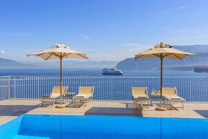 Área da piscina com espreguiçadeiras e guarda-sóis, com vista para um corpo d'água onde se avista um cruzeiro ao longe.