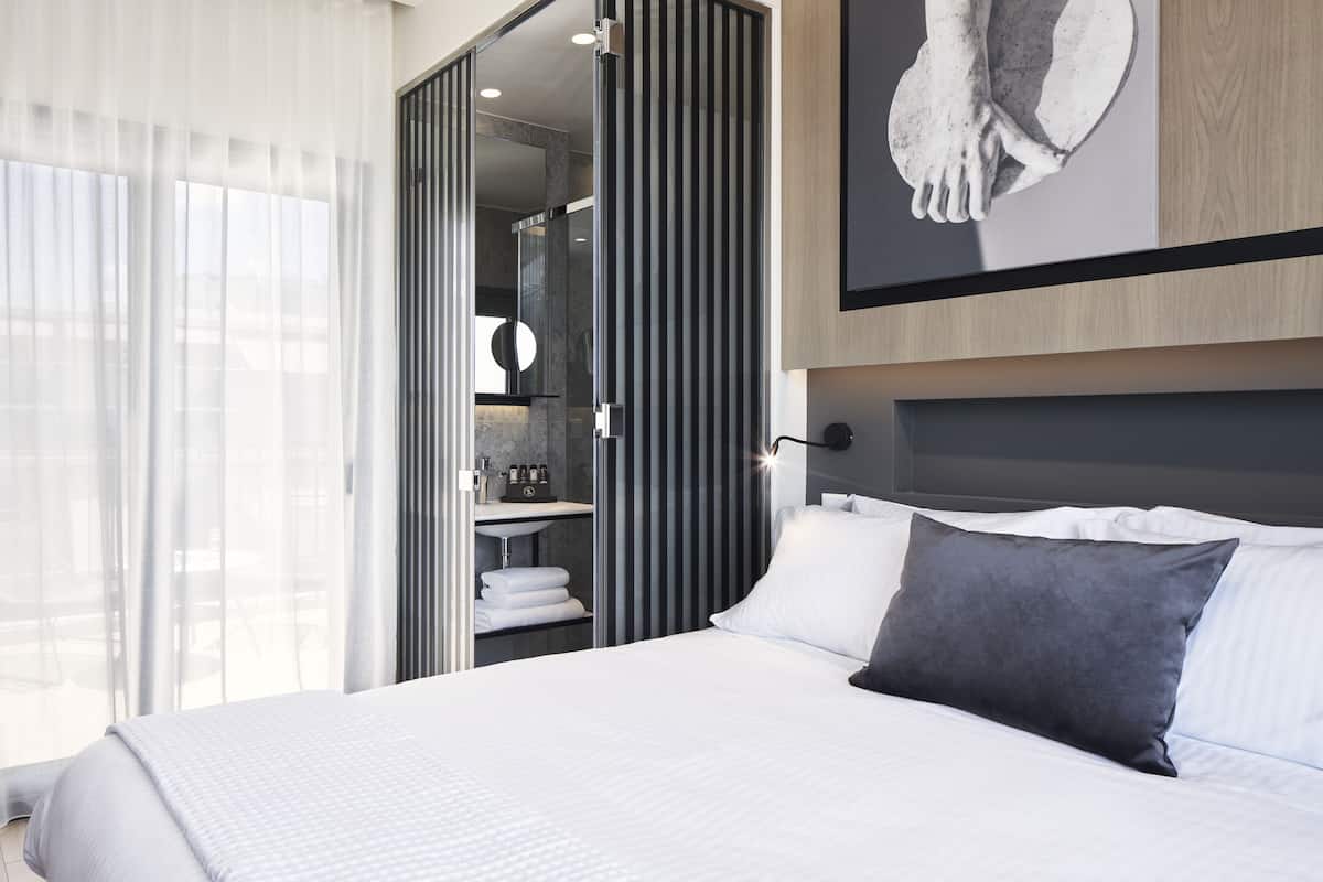 Quarto de hotel moderno com uma cama grande, um guarda-roupa e vista através de uma porta de vidro.