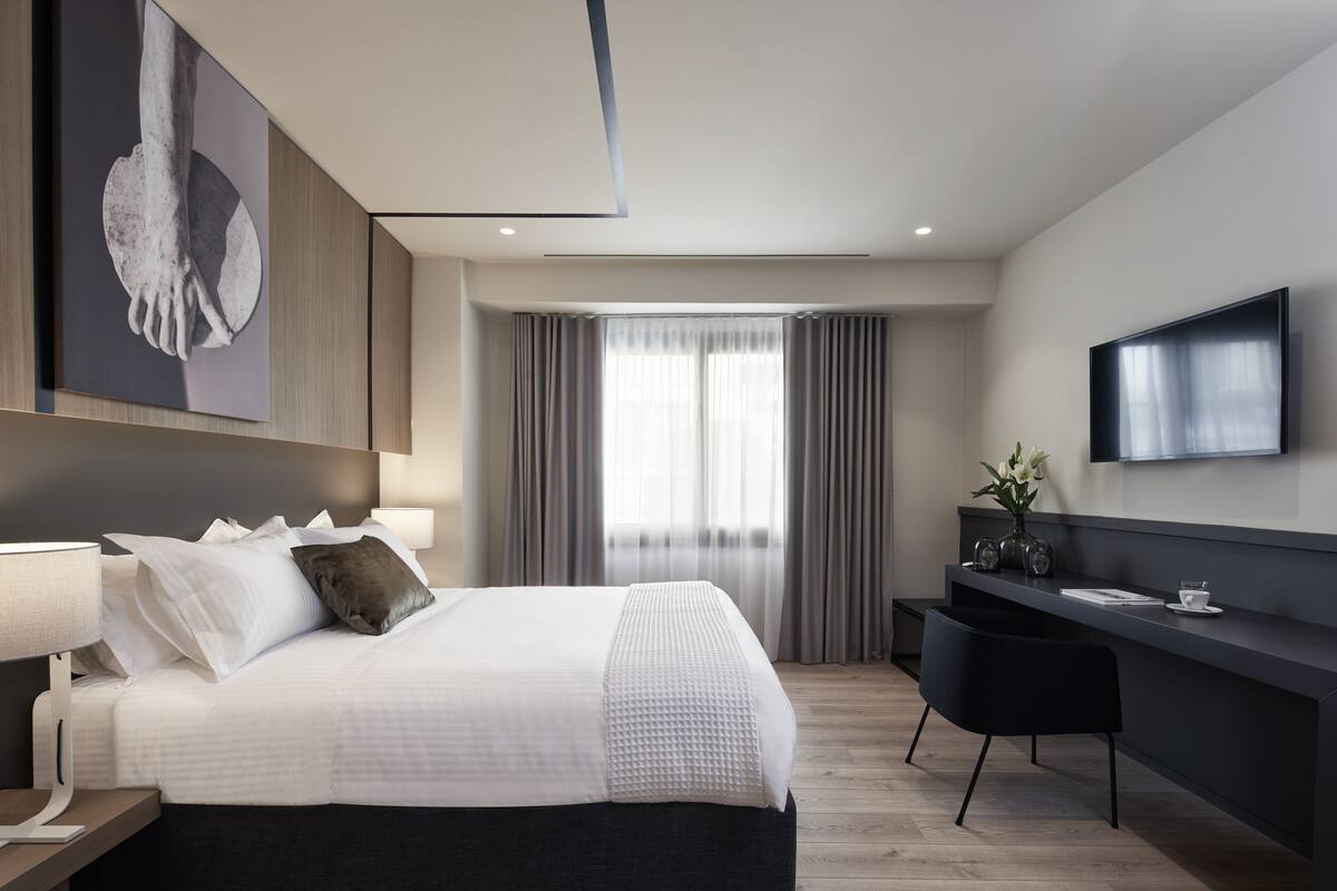 Quarto de hotel moderno com uma cama grande, uma escrivaninha e uma televisão.