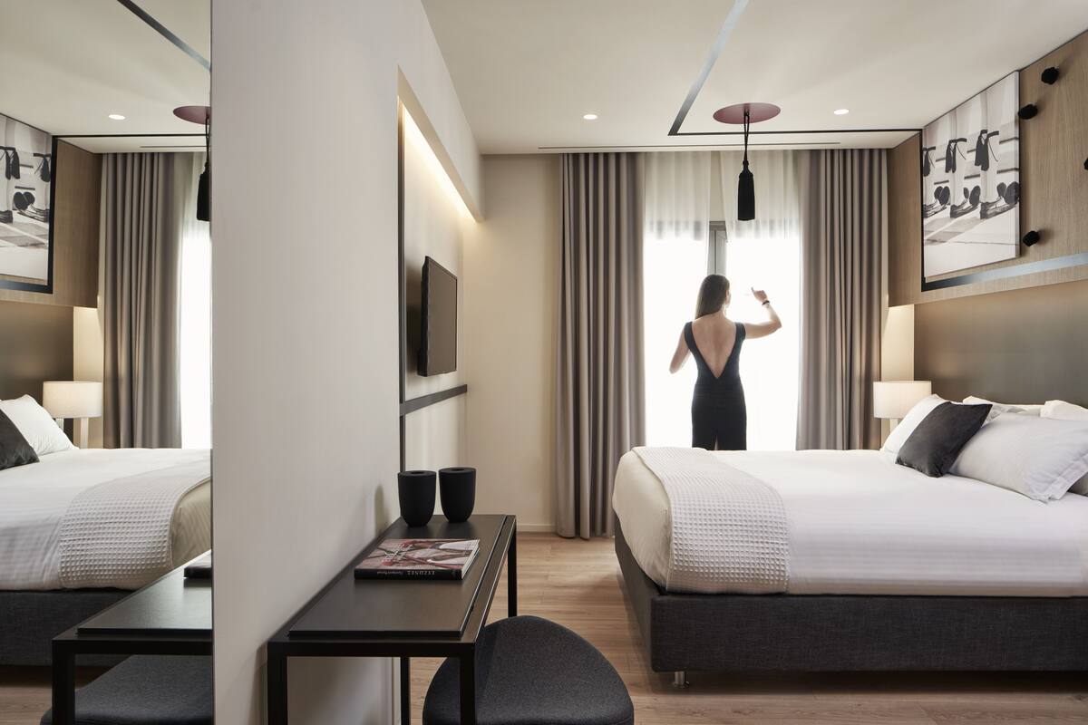 Quarto de hotel com duas camas, uma escrivaninha, uma cadeira, uma televisão e uma janela com cortinas.