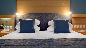 Quarto de hotel com uma cama grande, duas mesas de cabeceira, um criado-mudo e uma luminária fixada na parede.