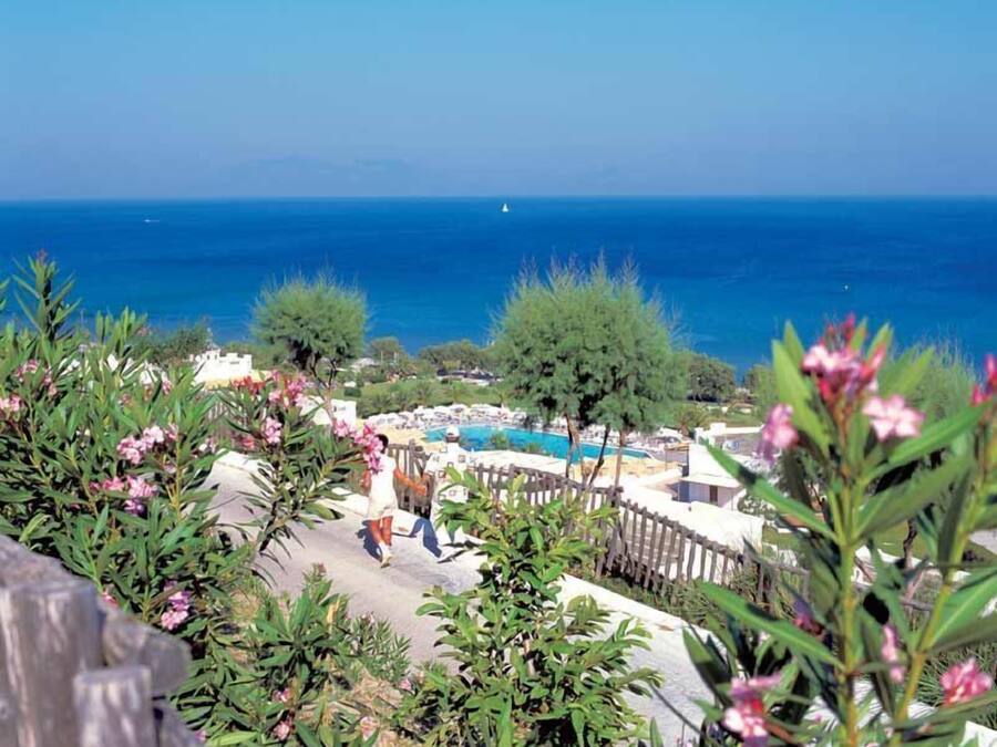 Um resort com piscina, vista para o mar e uma pessoa caminhando.