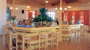 Uma área de bar com vários bancos, um balcão central e uma luminária decorativa no teto.