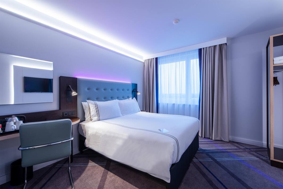 Quarto de hotel moderno com uma cama grande, escrivaninha, televisão de tela plana, cadeira e guarda-roupa.