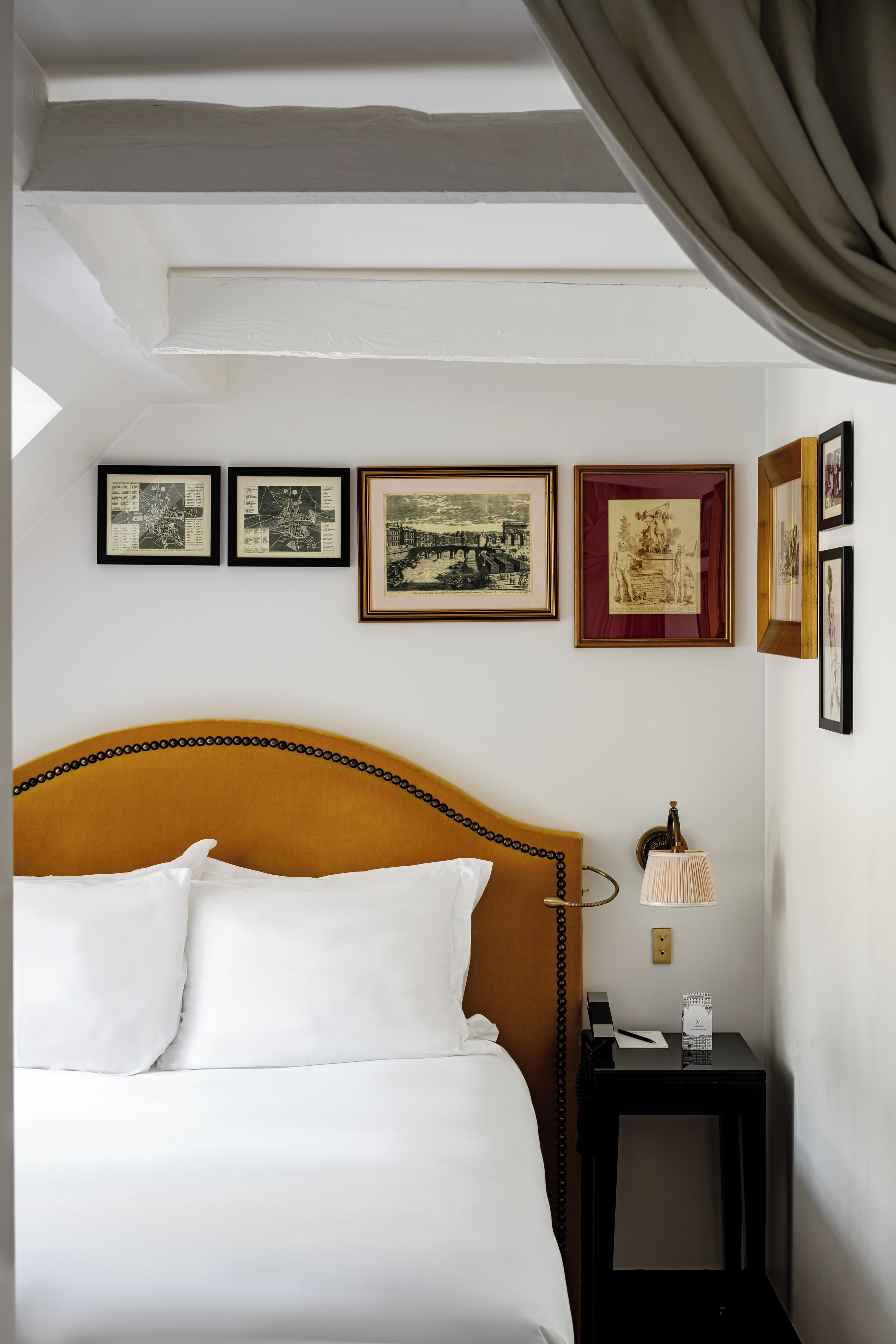 Quarto de hotel com cama, mesa de cabeceira e quadros na parede.