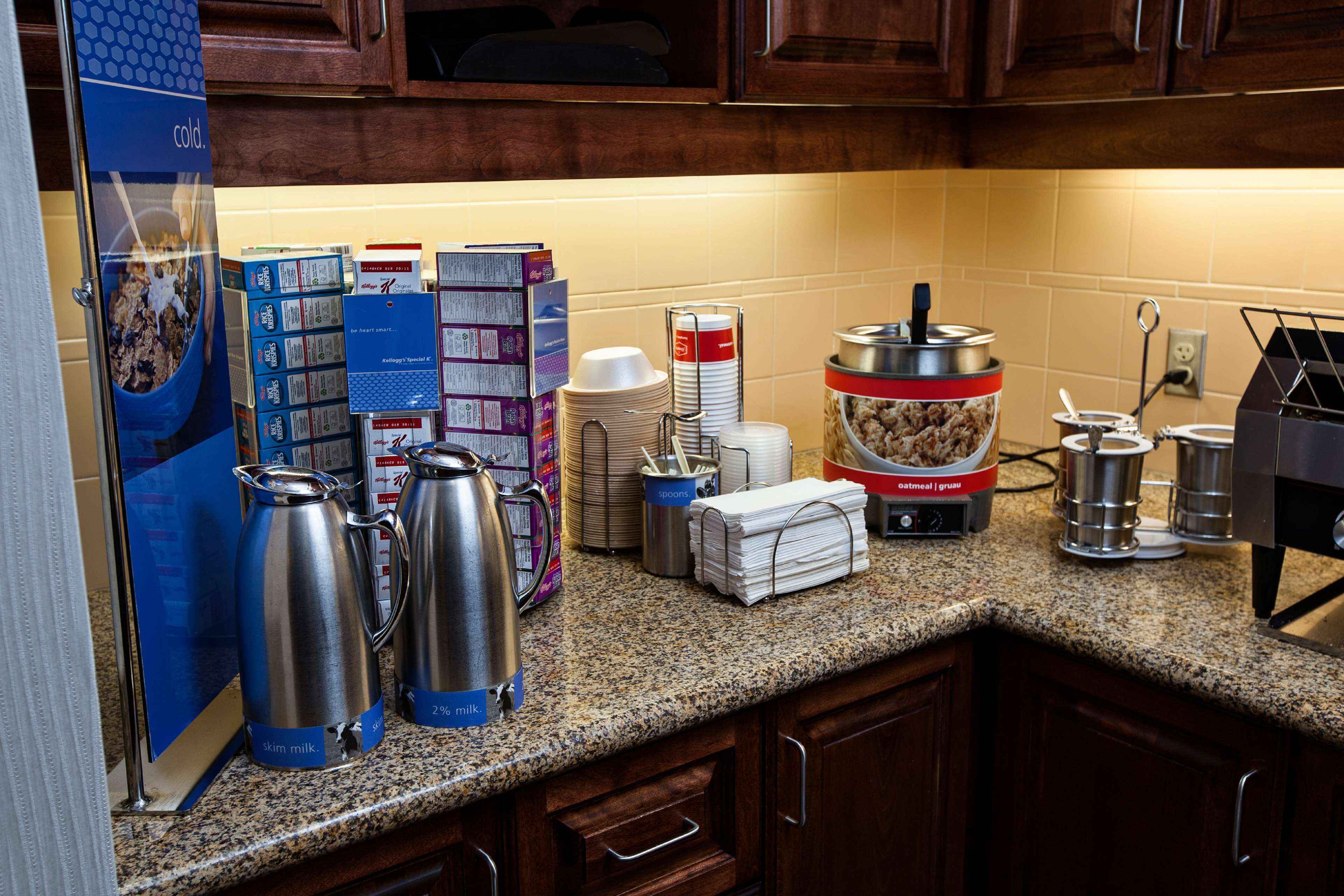 Uma bancada de cozinha com diversos itens de café da manhã, incluindo caixas de cereal, cafeteiras e um processador de alimentos.
