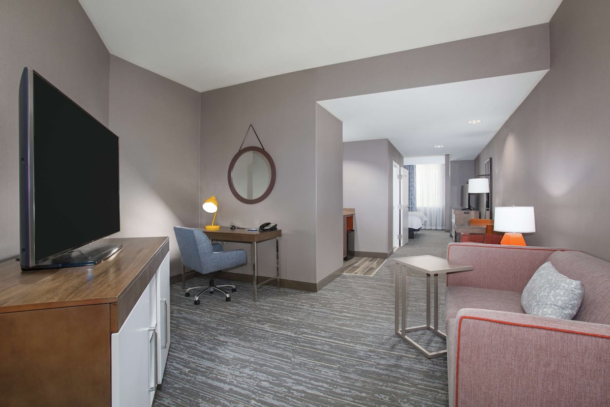Quarto de hotel com televisão de tela plana, uma escrivaninha com cadeira, um sofá e um espelho na parede.