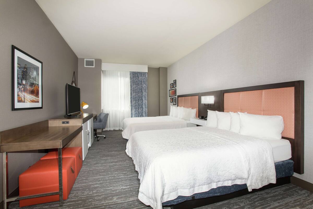 Quarto de hotel com duas camas, uma mesa de escritório com computador, televisão e janela com cortinas.